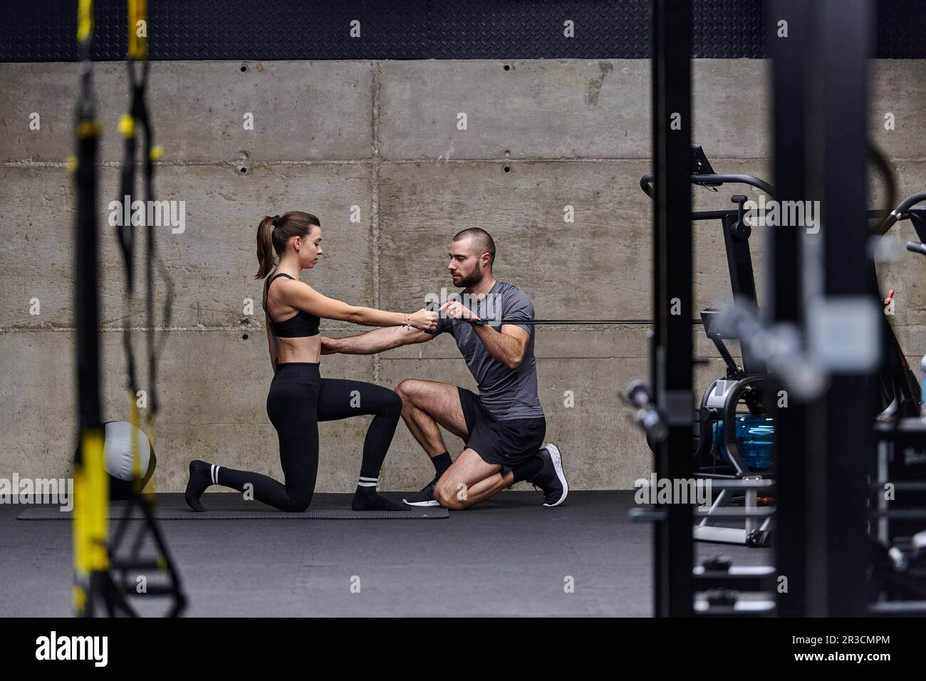 A muscular man assisting a fit woman in a modern gym as they engage in ...