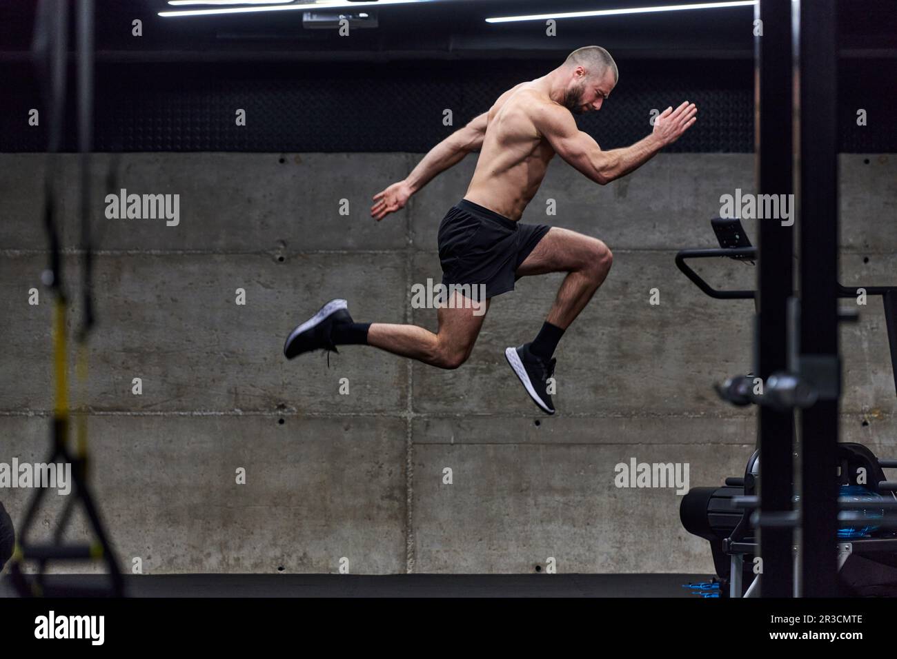 A muscular man captured in air as he jumps in a modern gym, showcasing ...