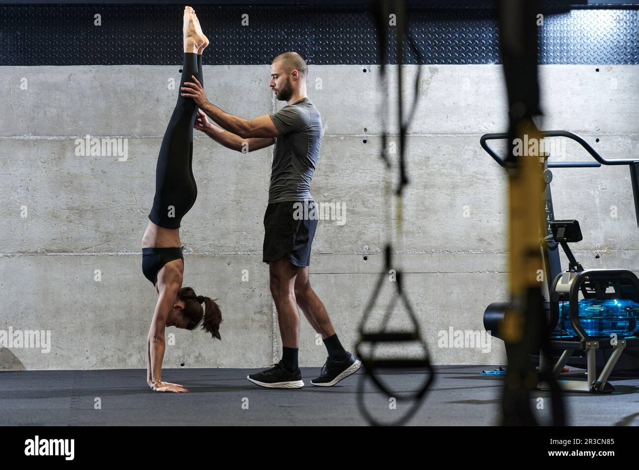 A muscular man assisting a fit woman in a modern gym as they engage in ...