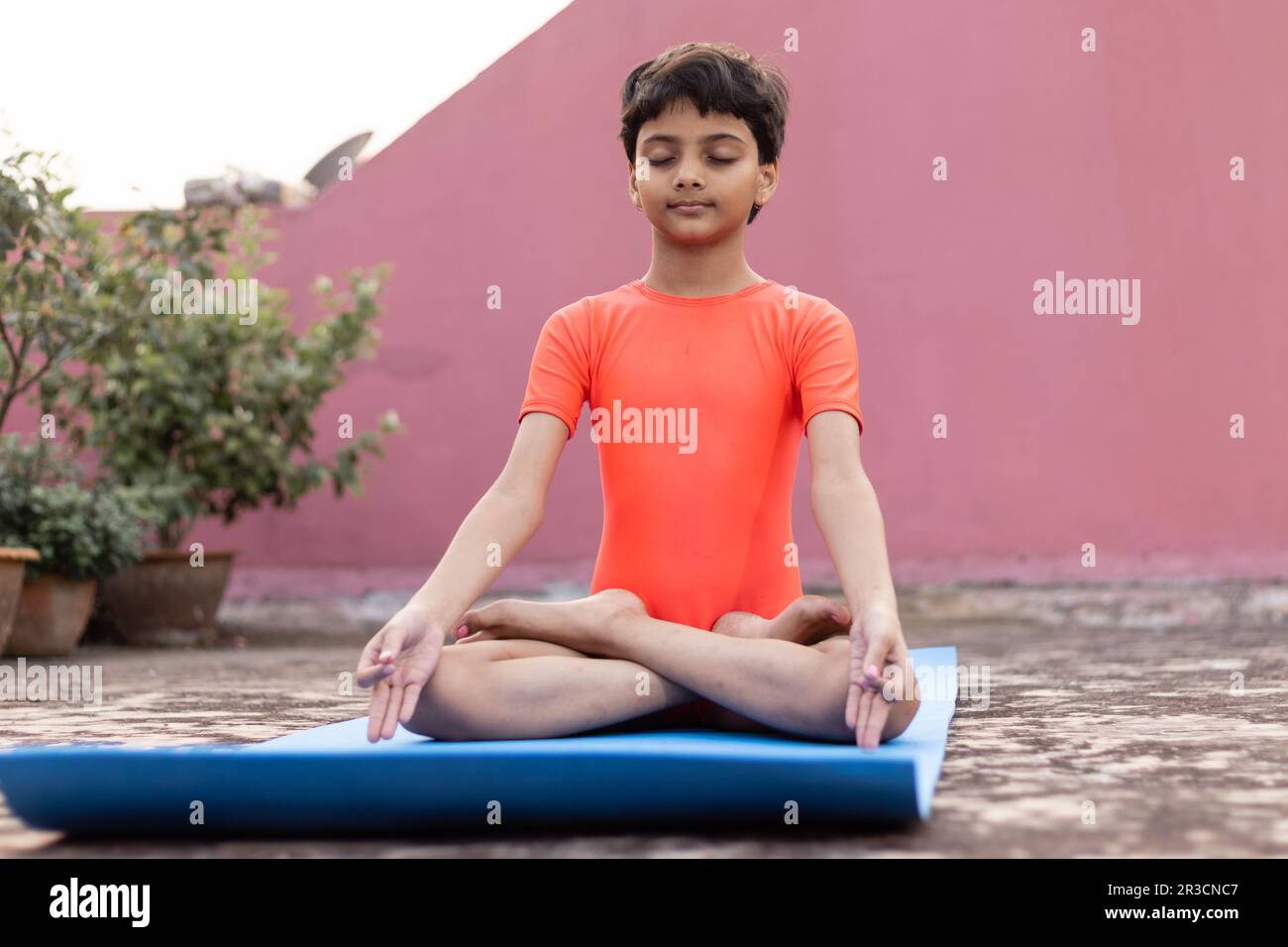An Indian girl child practicing yoga padmasana on yoga mat outdoors ...