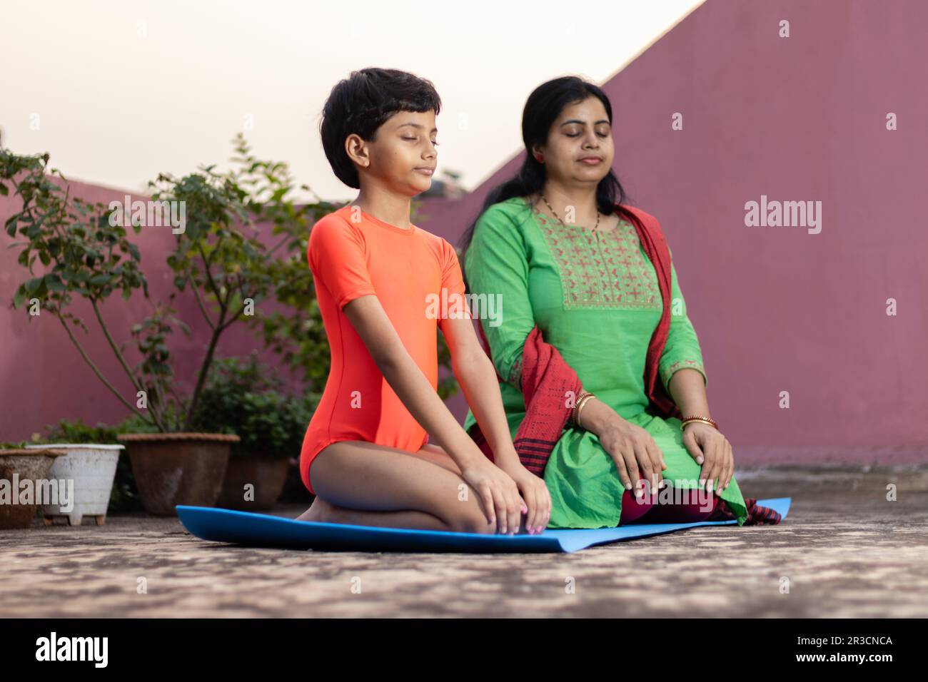 An Indian girl child with mother practicing Vajrasana yoga on yoga mat ...