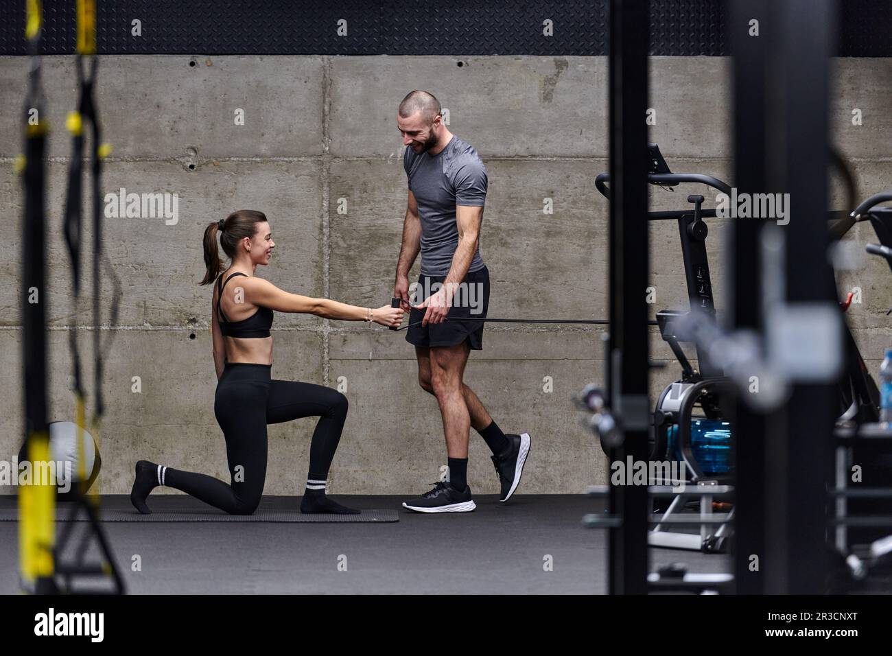 A muscular man assisting a fit woman in a modern gym as they engage in ...