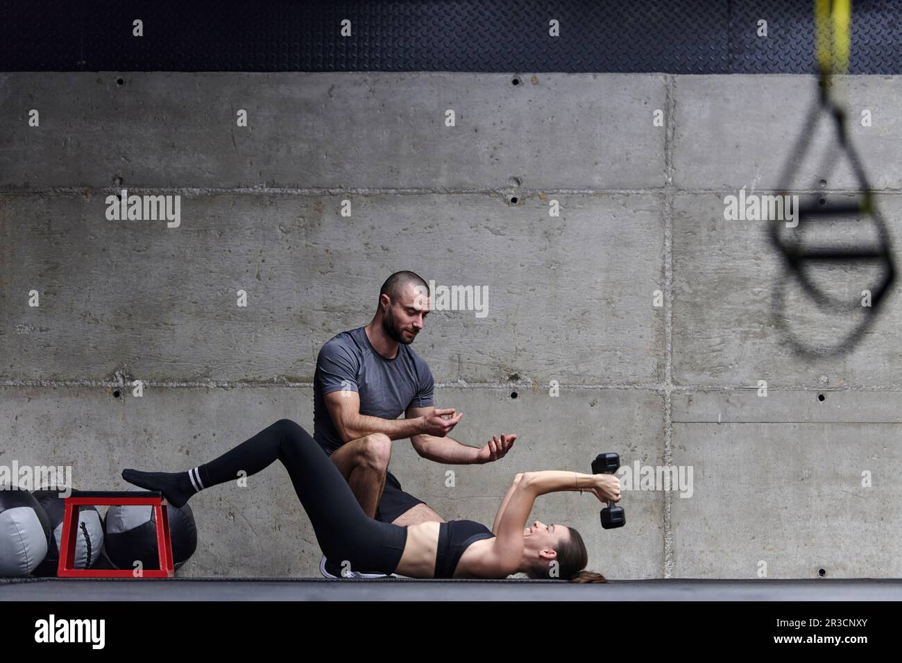 A muscular man assisting a fit woman in a modern gym as they engage in ...