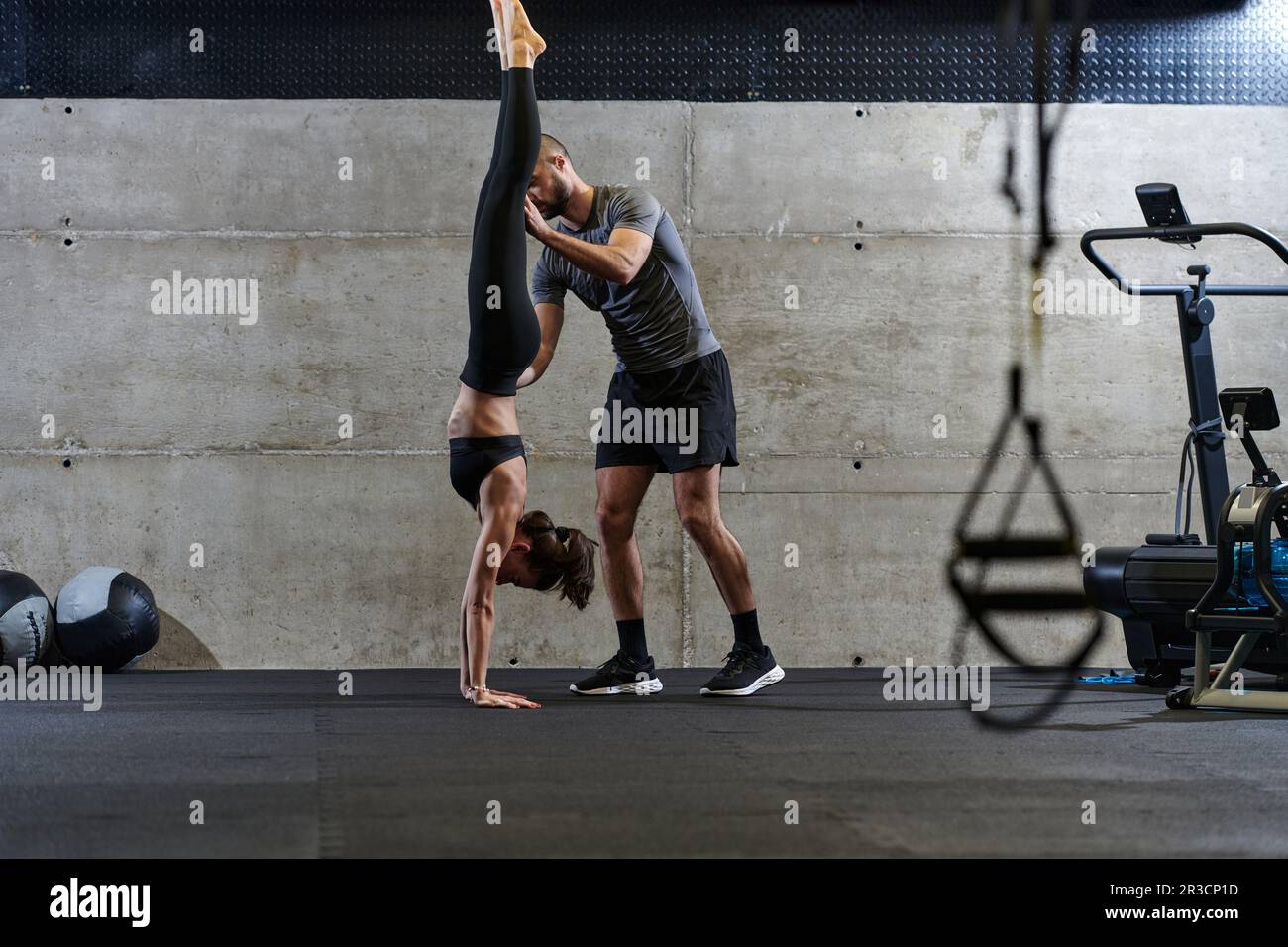 A muscular man assisting a fit woman in a modern gym as they engage in ...