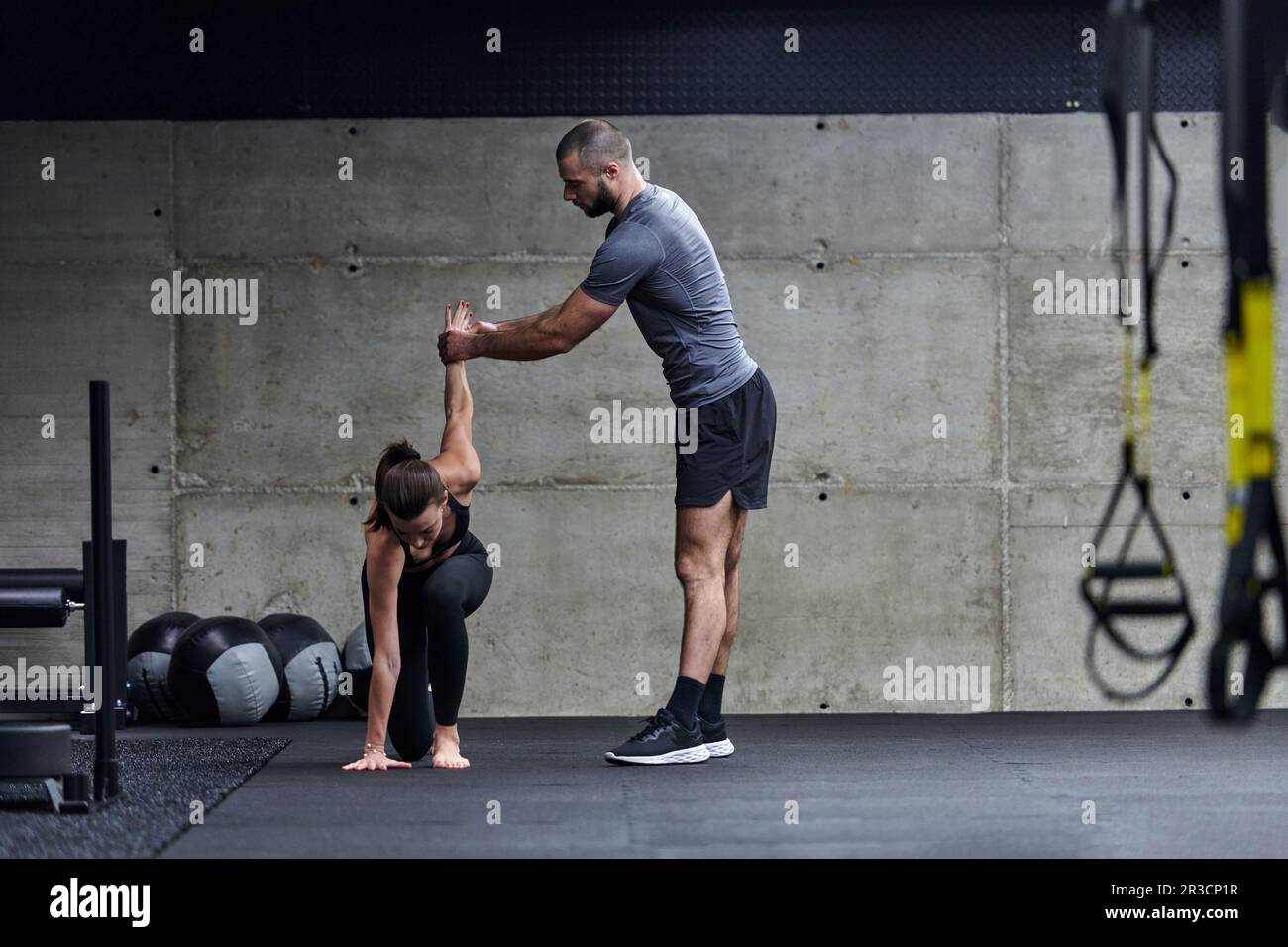 A muscular man assisting a fit woman in a modern gym as they engage in ...