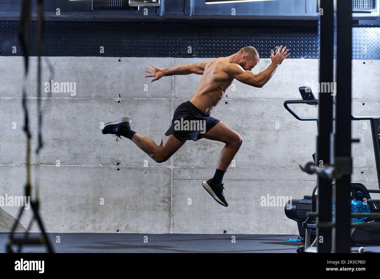 A muscular man captured in air as he jumps in a modern gym, showcasing ...