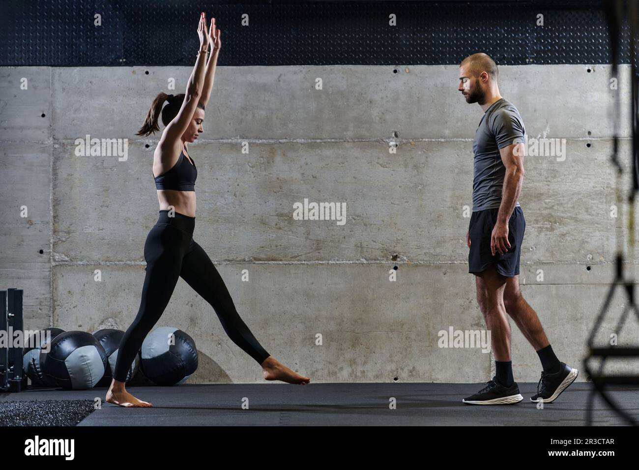 A muscular man assisting a fit woman in a modern gym as they engage in ...