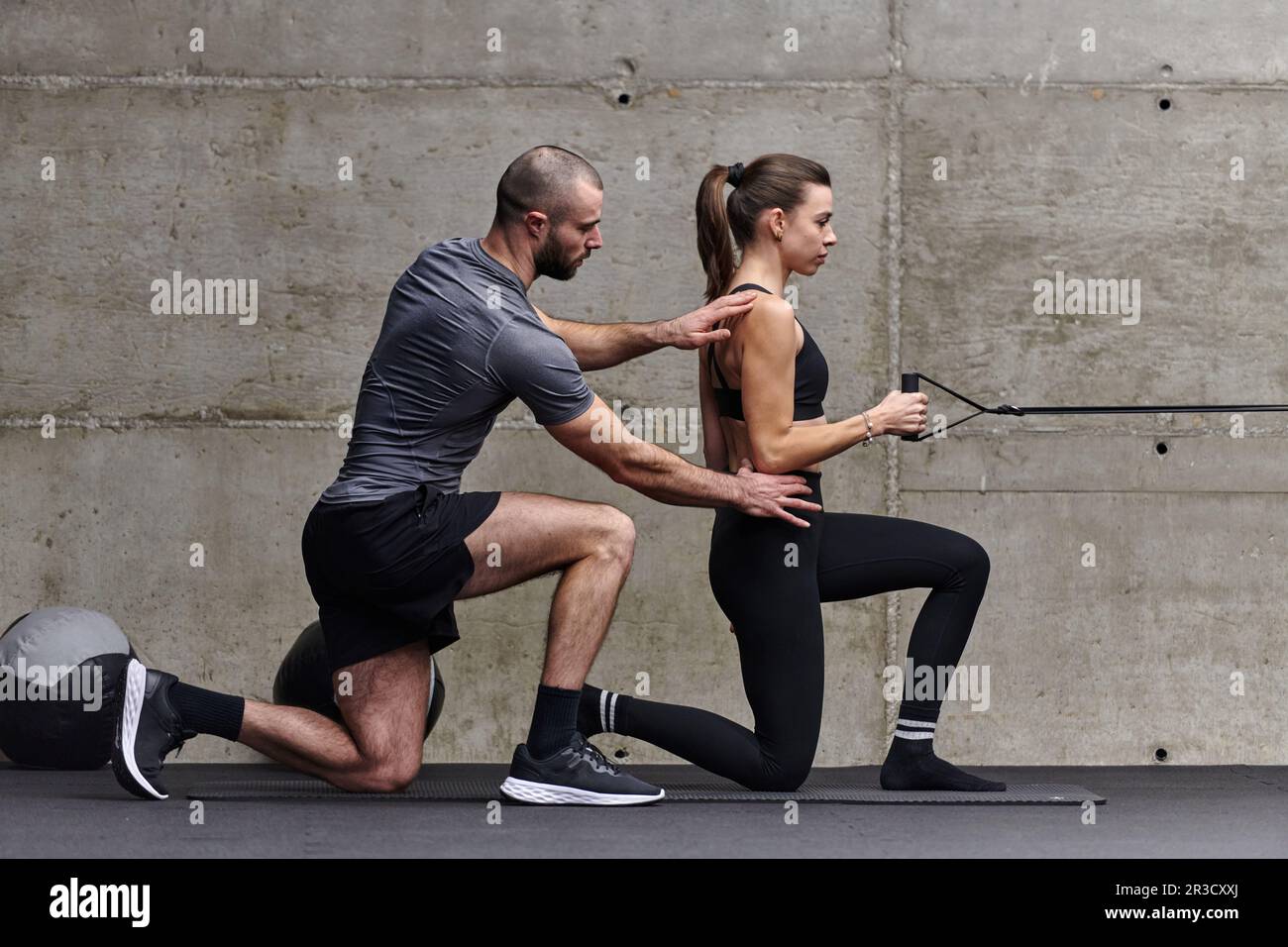 A muscular man assisting a fit woman in a modern gym as they engage in ...