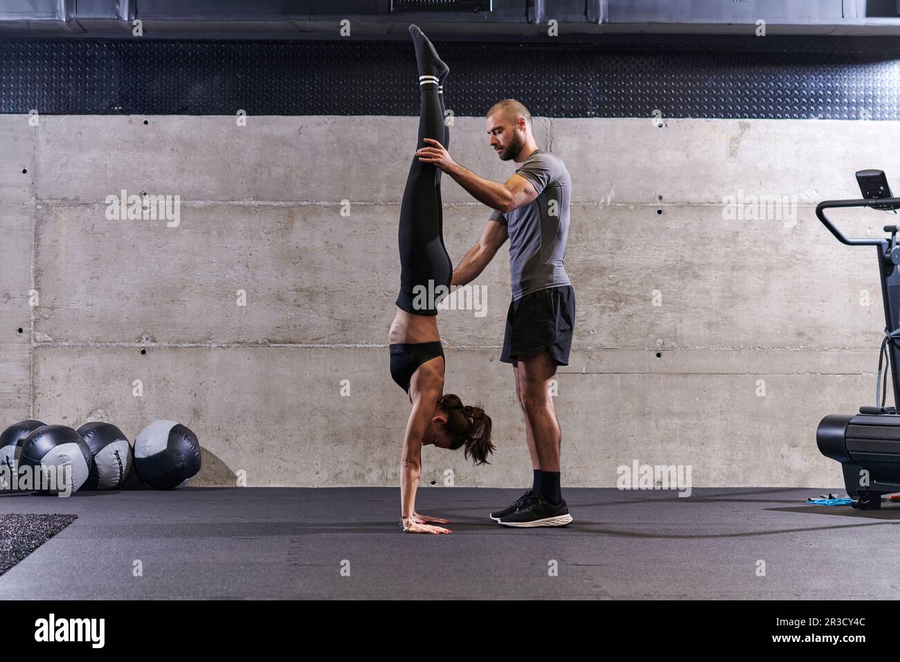A muscular man assisting a fit woman in a modern gym as they engage in ...