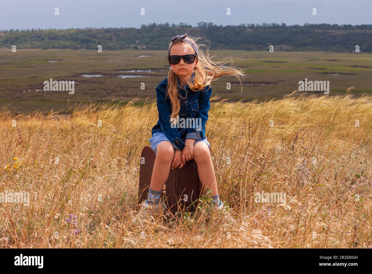 Little Blonde Girl In Denim Jacket Black Sunglasses Blue Dress With Vintage Suitcase In Wild