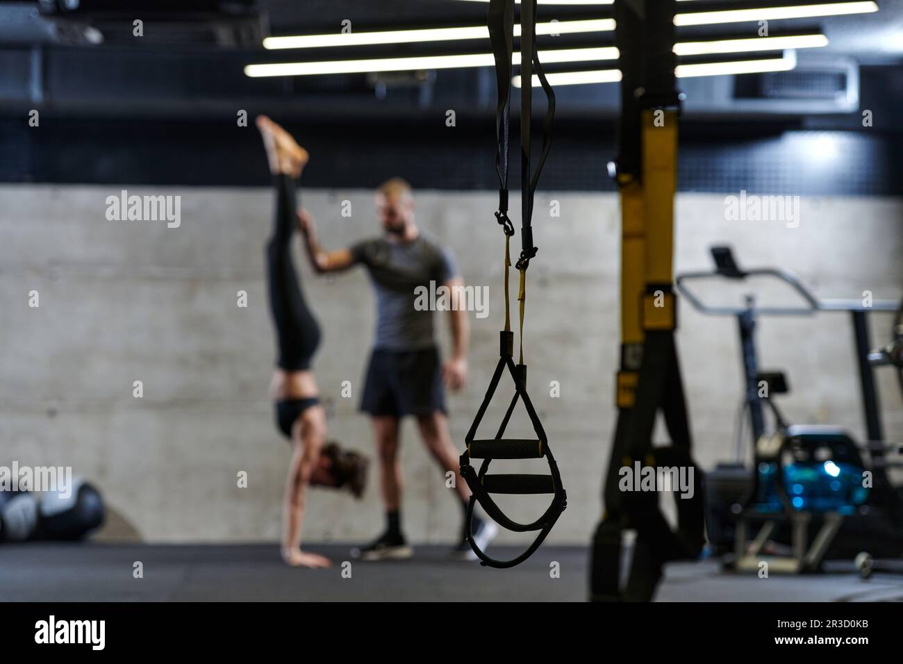 A muscular man assisting a fit woman in a modern gym as they engage in ...