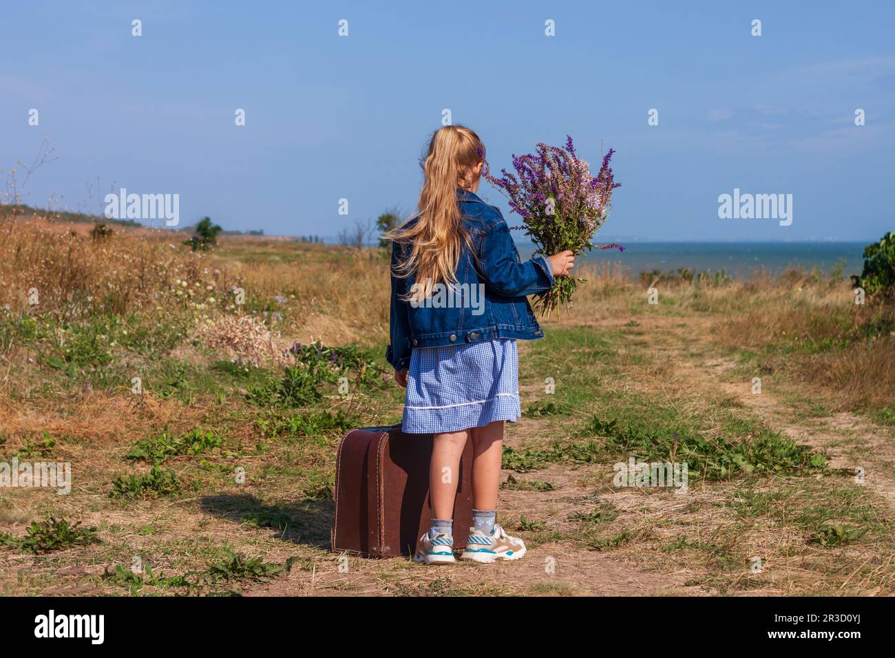 Little Blonde Girl In Denim Jacket Blue Dress With Vintage Suitcase And Flowers Bouquet Off