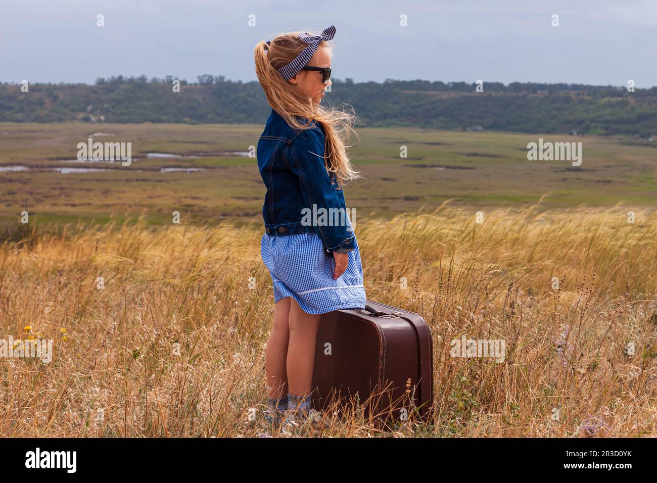 Little Blonde Girl In Denim Jacket Black Sunglasses Blue Dress With Vintage Suitcase In Wild