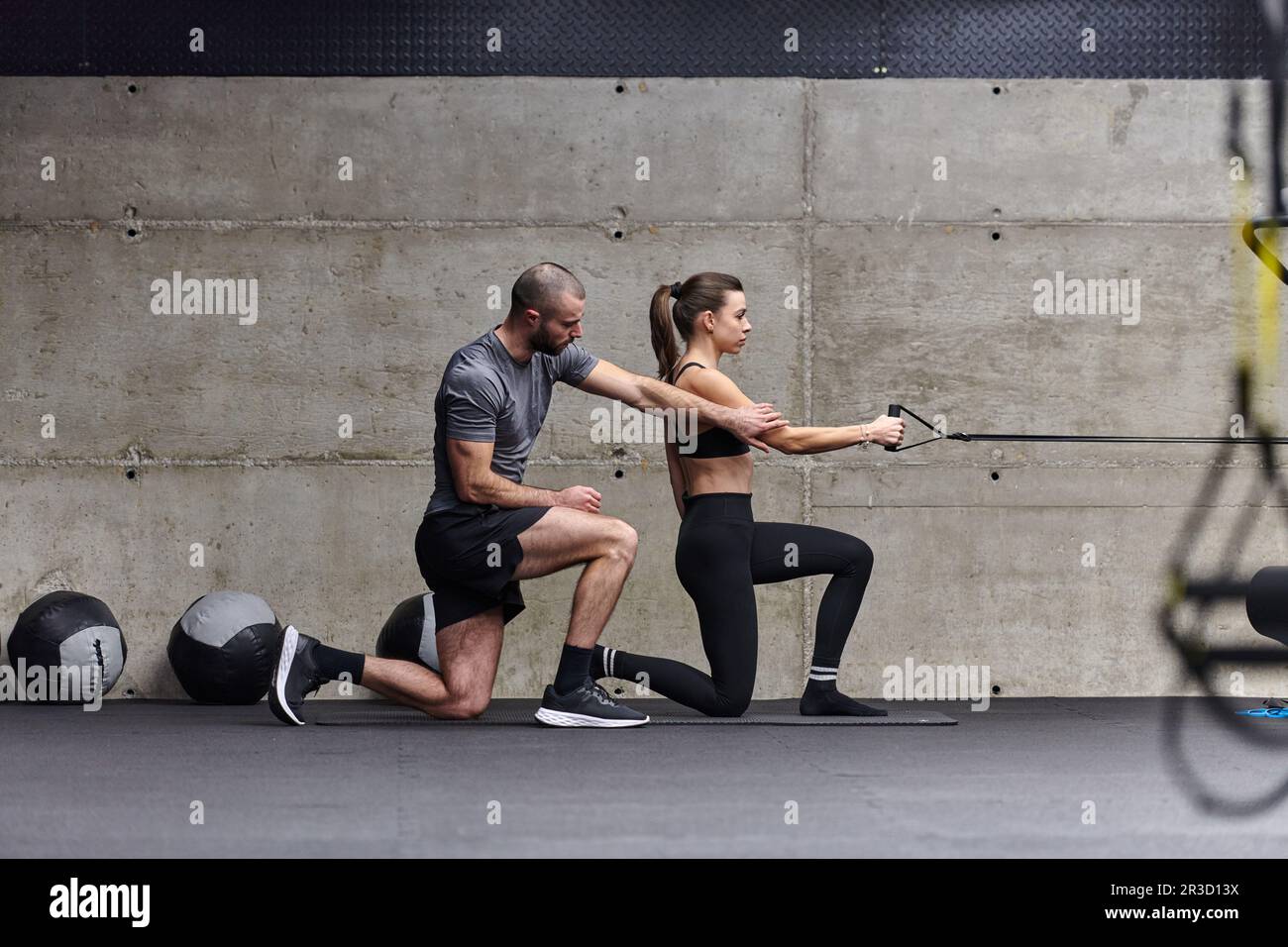 A muscular man assisting a fit woman in a modern gym as they engage in ...