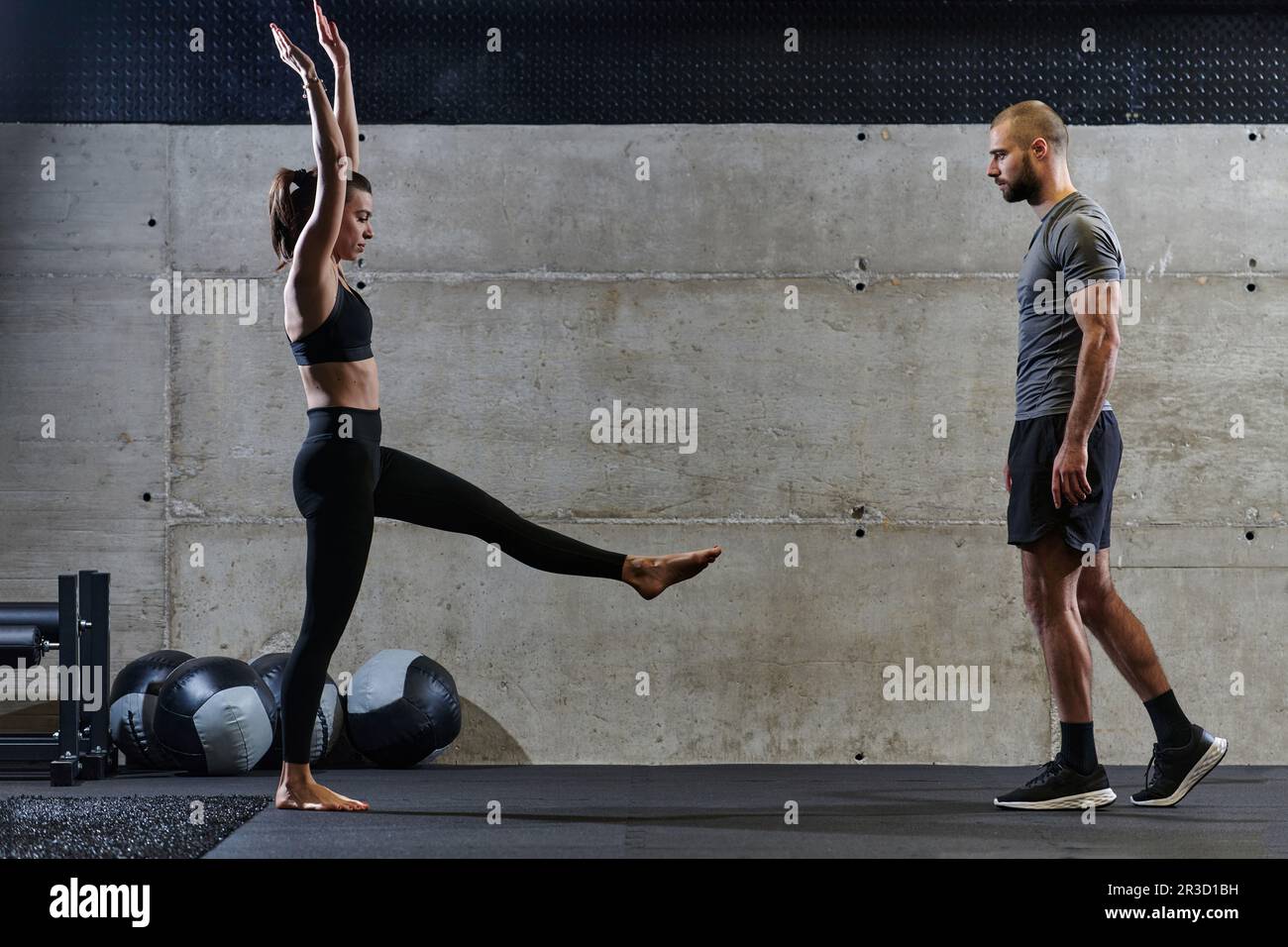 A muscular man assisting a fit woman in a modern gym as they engage in ...