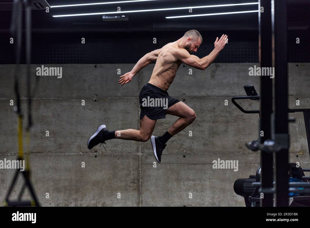 A muscular man captured in air as he jumps in a modern gym, showcasing ...