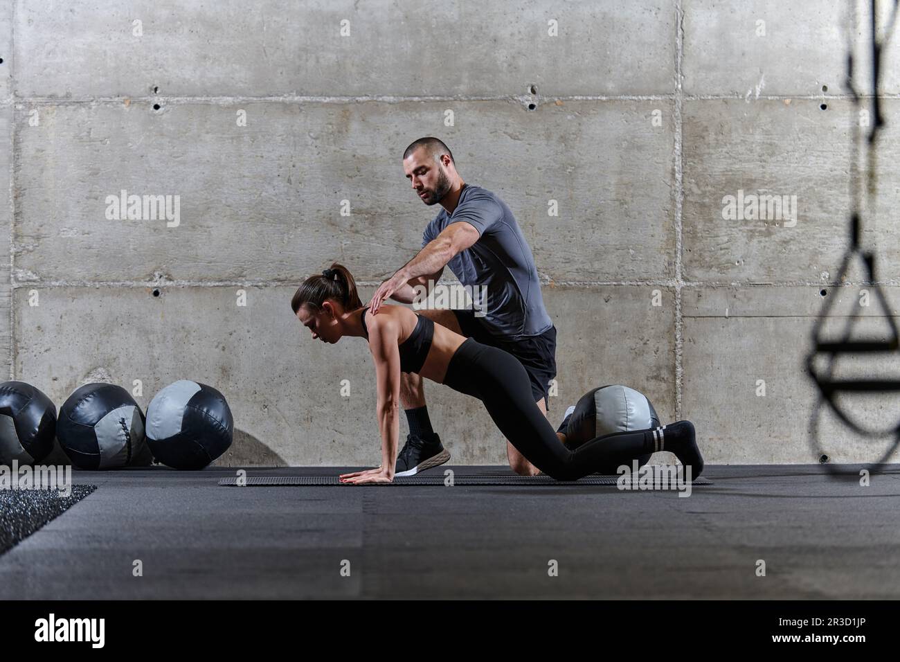 A muscular man assisting a fit woman in a modern gym as they engage in ...
