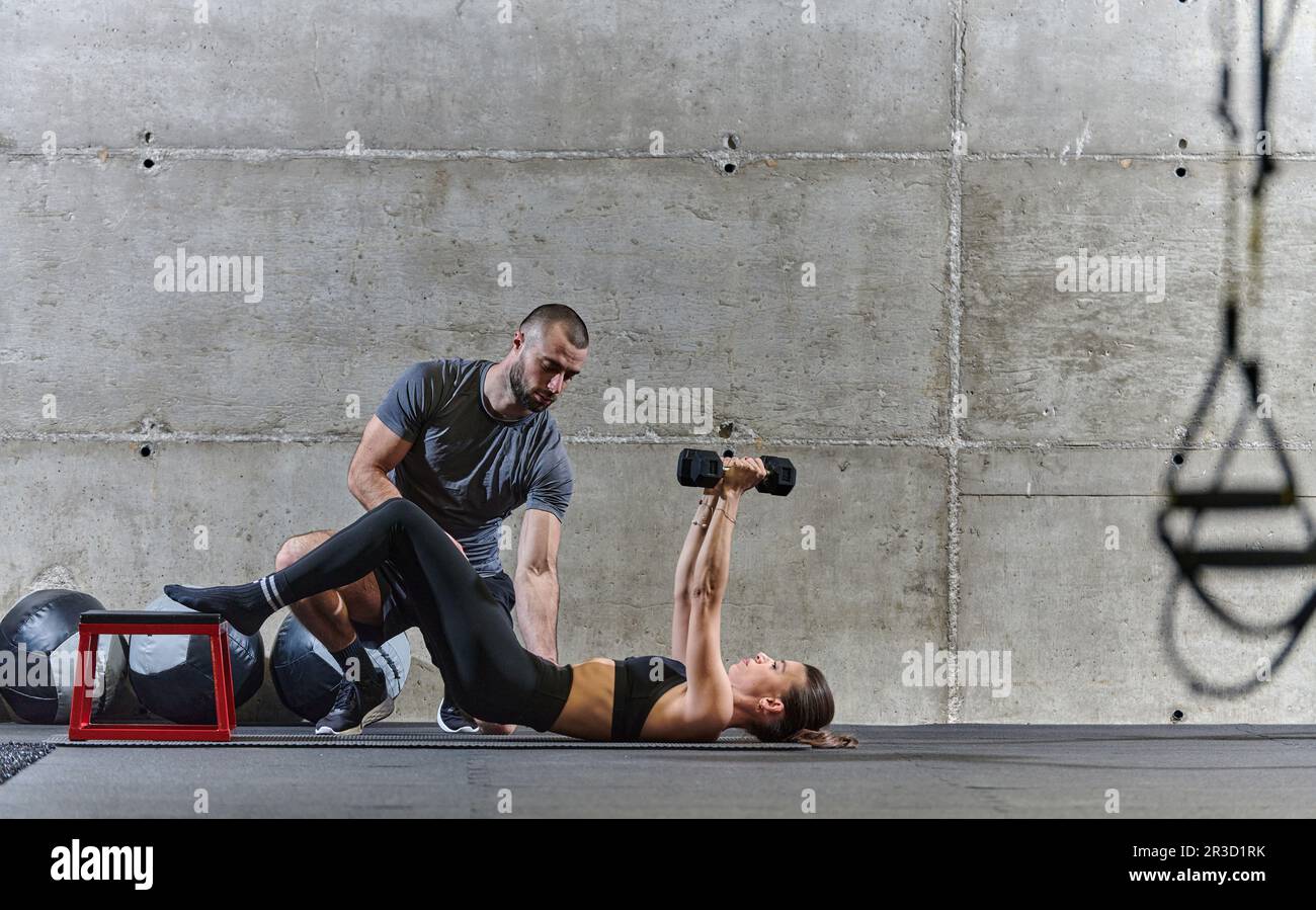 A muscular man assisting a fit woman in a modern gym as they engage in ...
