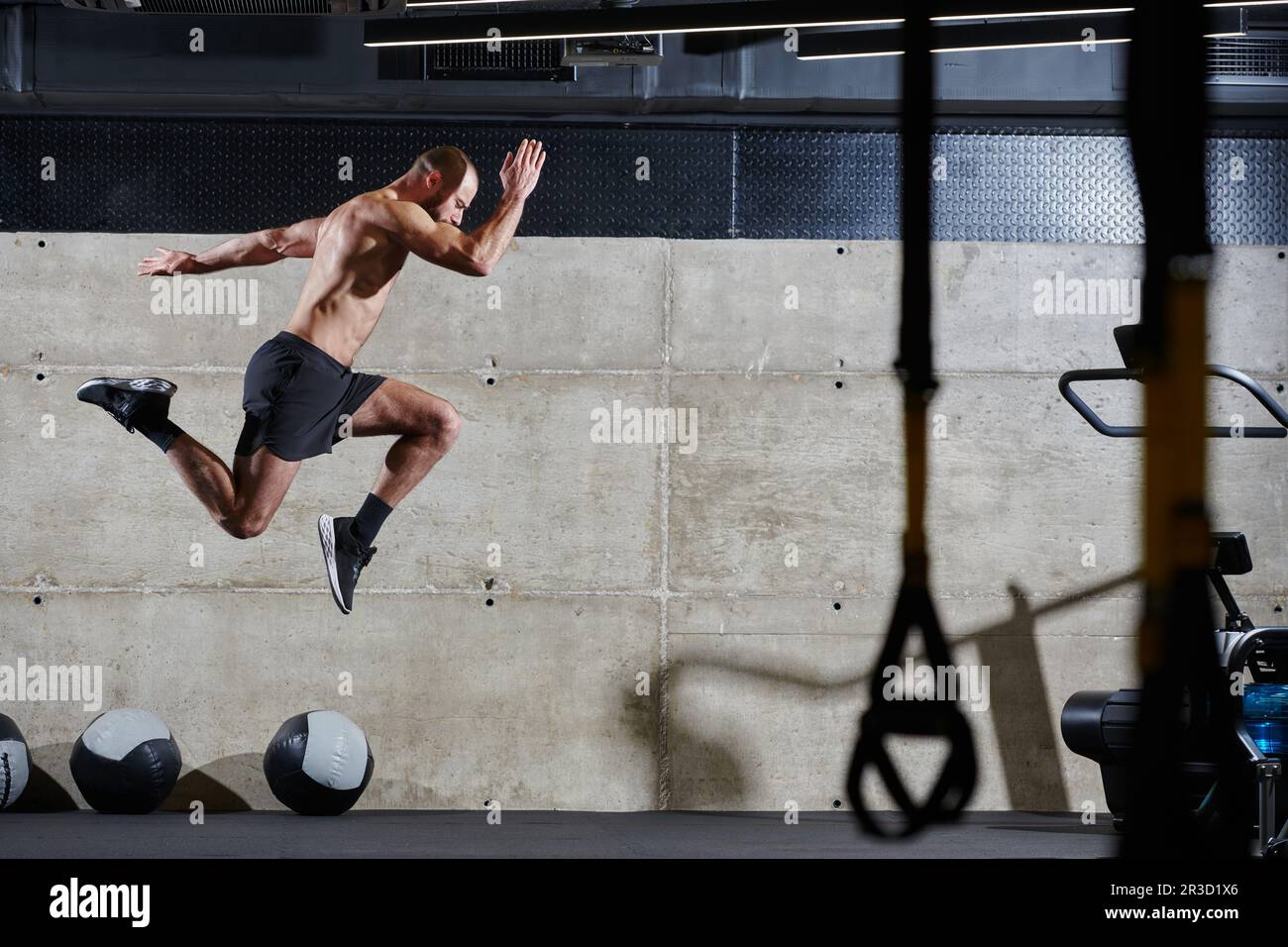 A muscular man captured in air as he jumps in a modern gym, showcasing ...