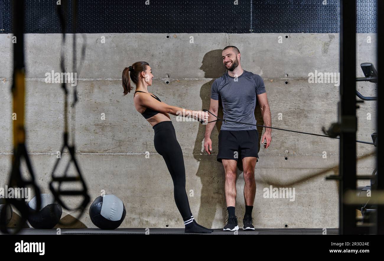 A muscular man assisting a fit woman in a modern gym as they engage in ...