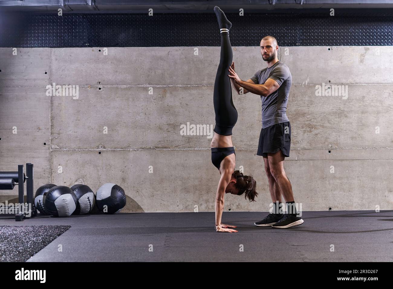 A muscular man assisting a fit woman in a modern gym as they engage in ...