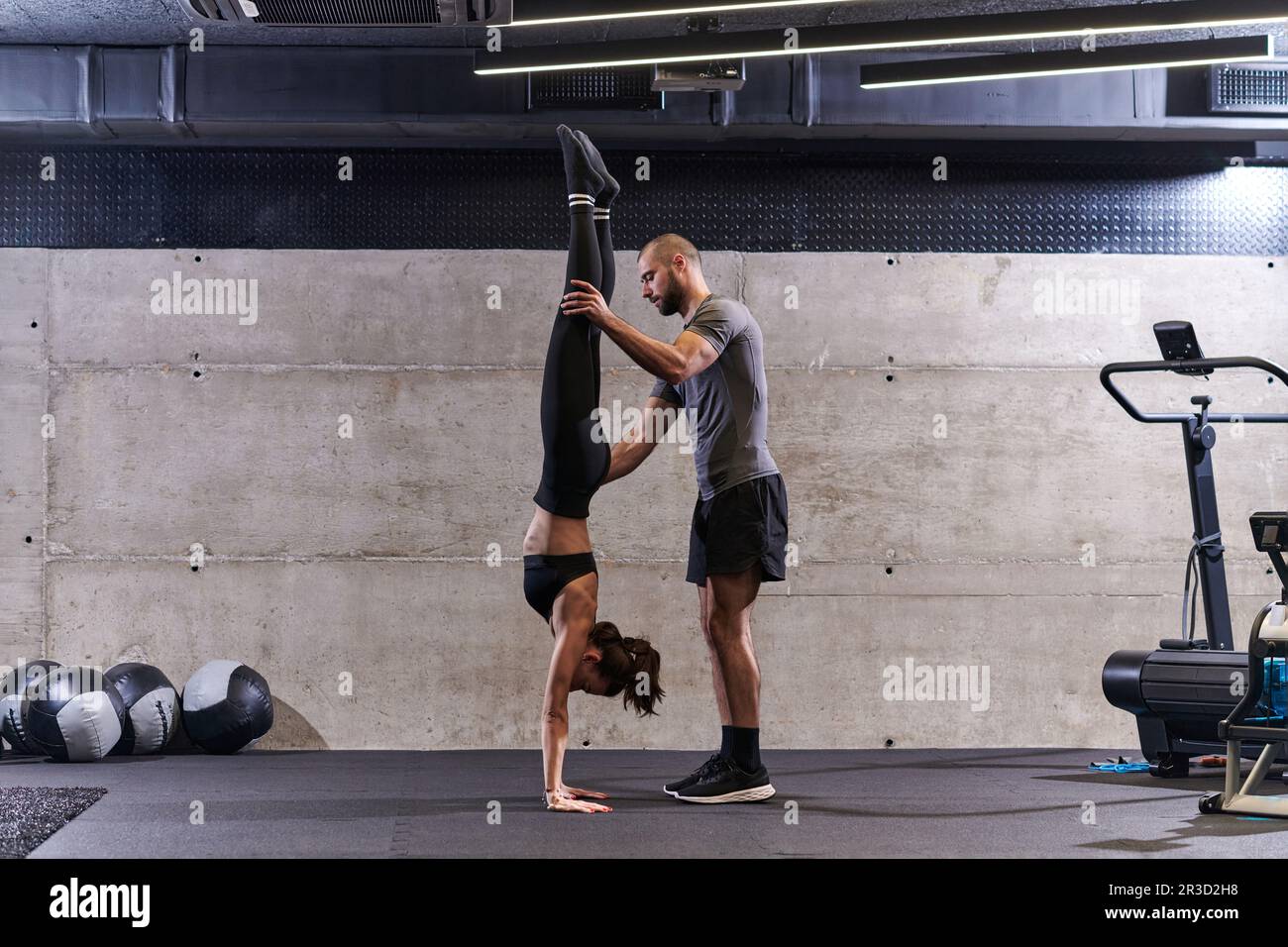 A muscular man assisting a fit woman in a modern gym as they engage in ...