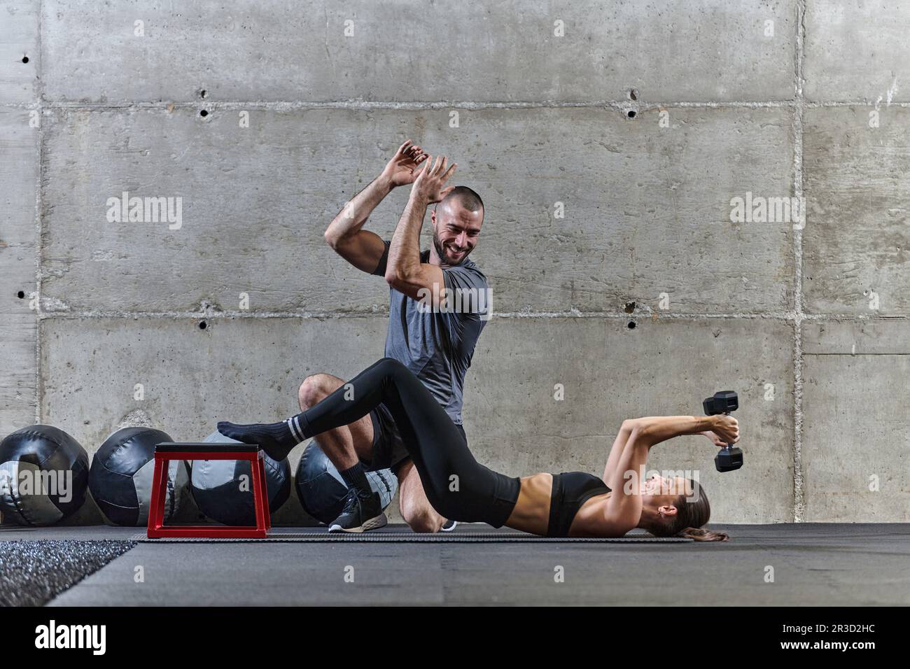 A muscular man assisting a fit woman in a modern gym as they engage in ...