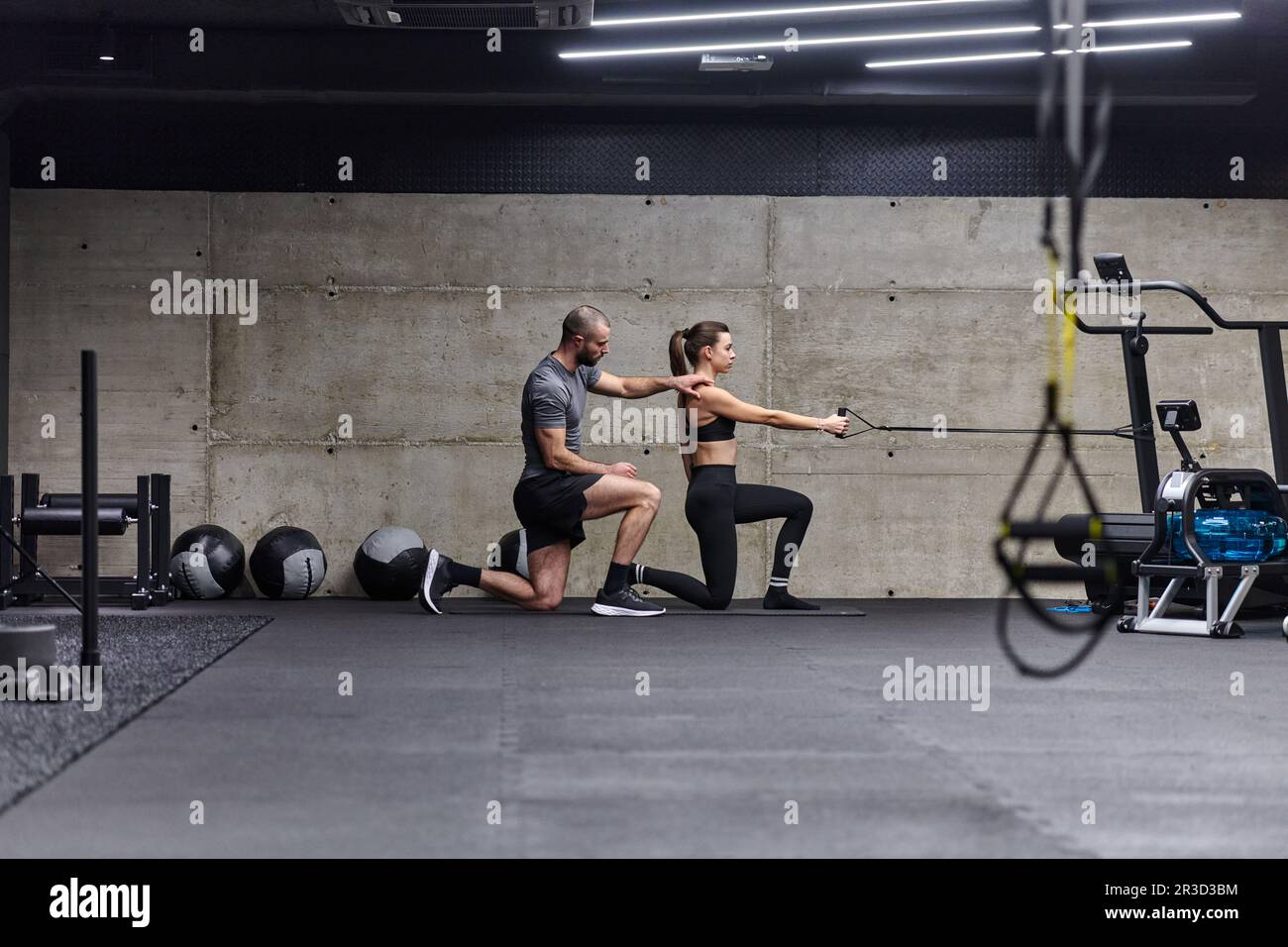A muscular man assisting a fit woman in a modern gym as they engage in ...