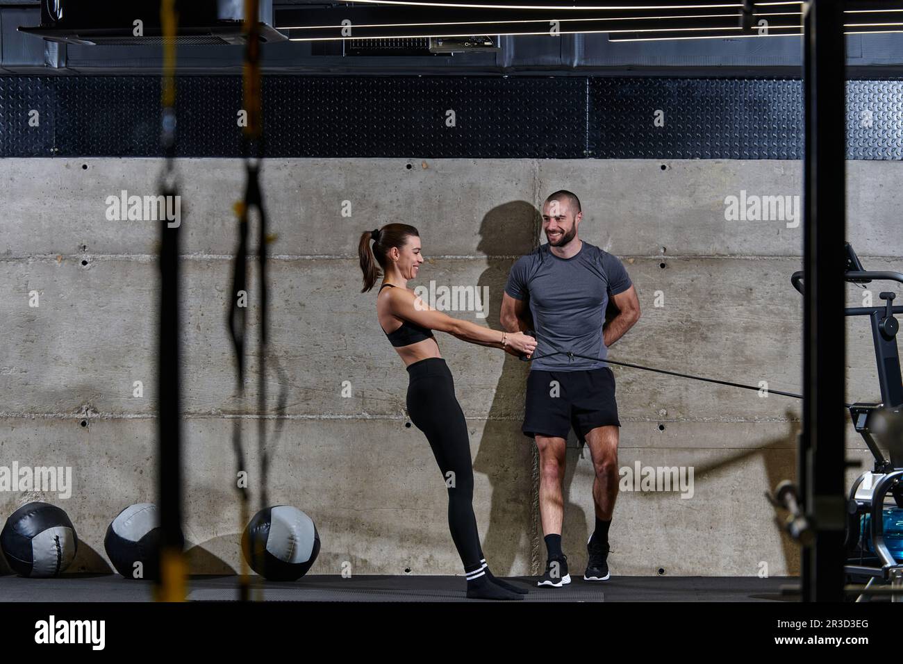 A muscular man assisting a fit woman in a modern gym as they engage in ...