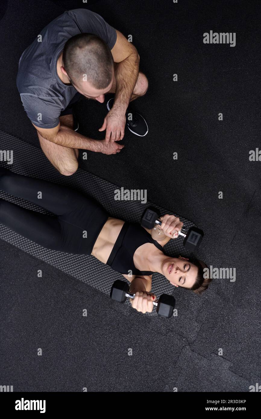 A muscular man assisting a fit woman in a modern gym as they engage in ...