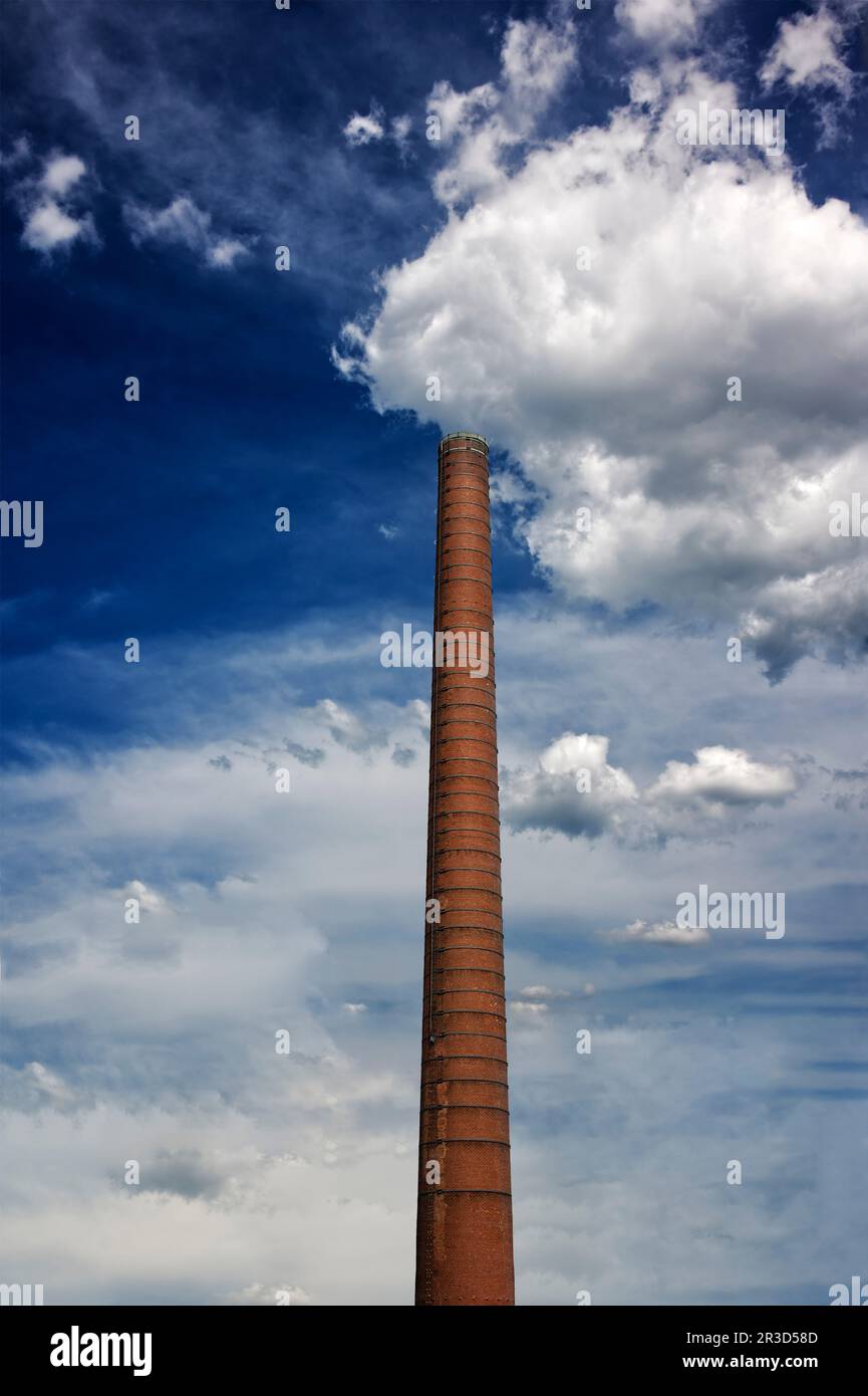 An ancient high chimney of an old fabric reaches the cloudy blue sky ...