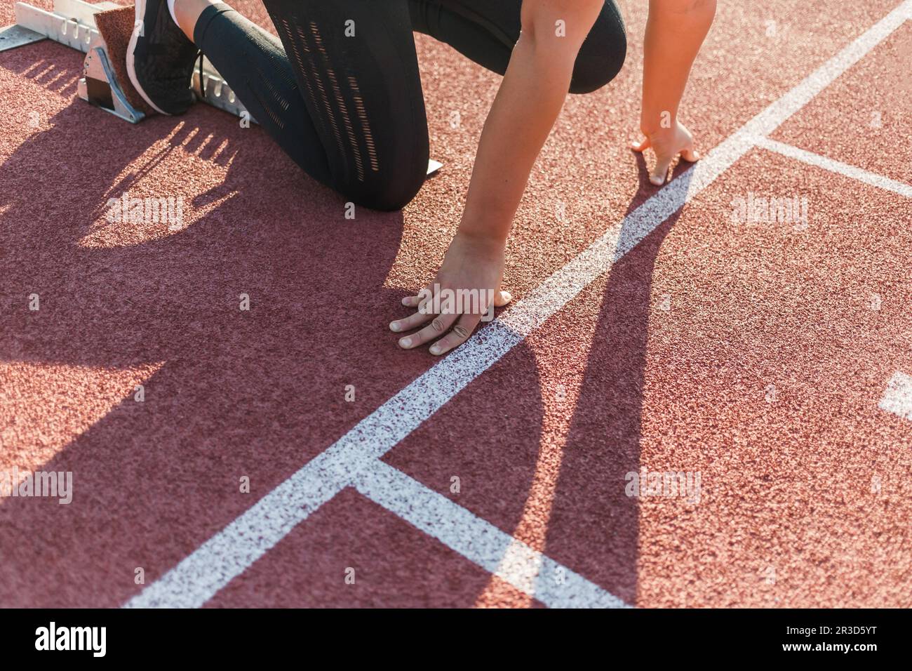 Caucasian woman at the athletic track starting point, hands on the ...