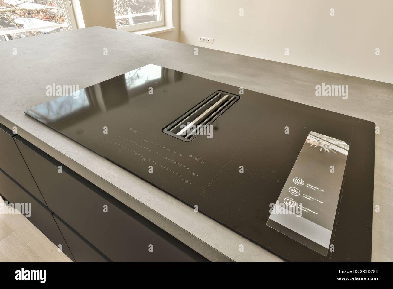 a black stove top on a kitchen counter with an oven in the background ...