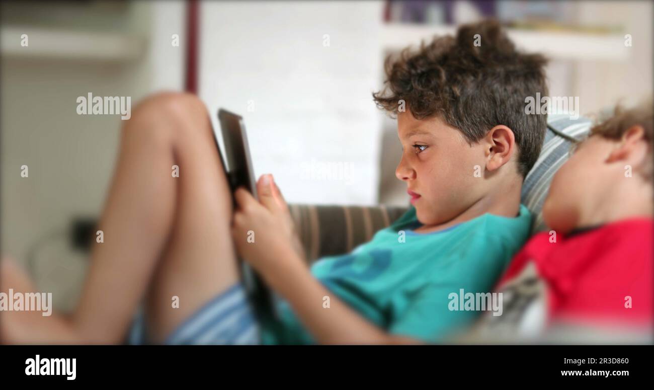 Child using tablet tech device at home. Candid kids playing game ...