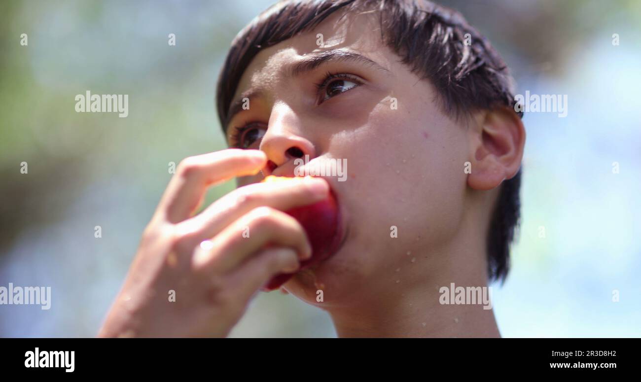 Child eating peach fruit outdoors taking a bite of healthy snack Stock ...
