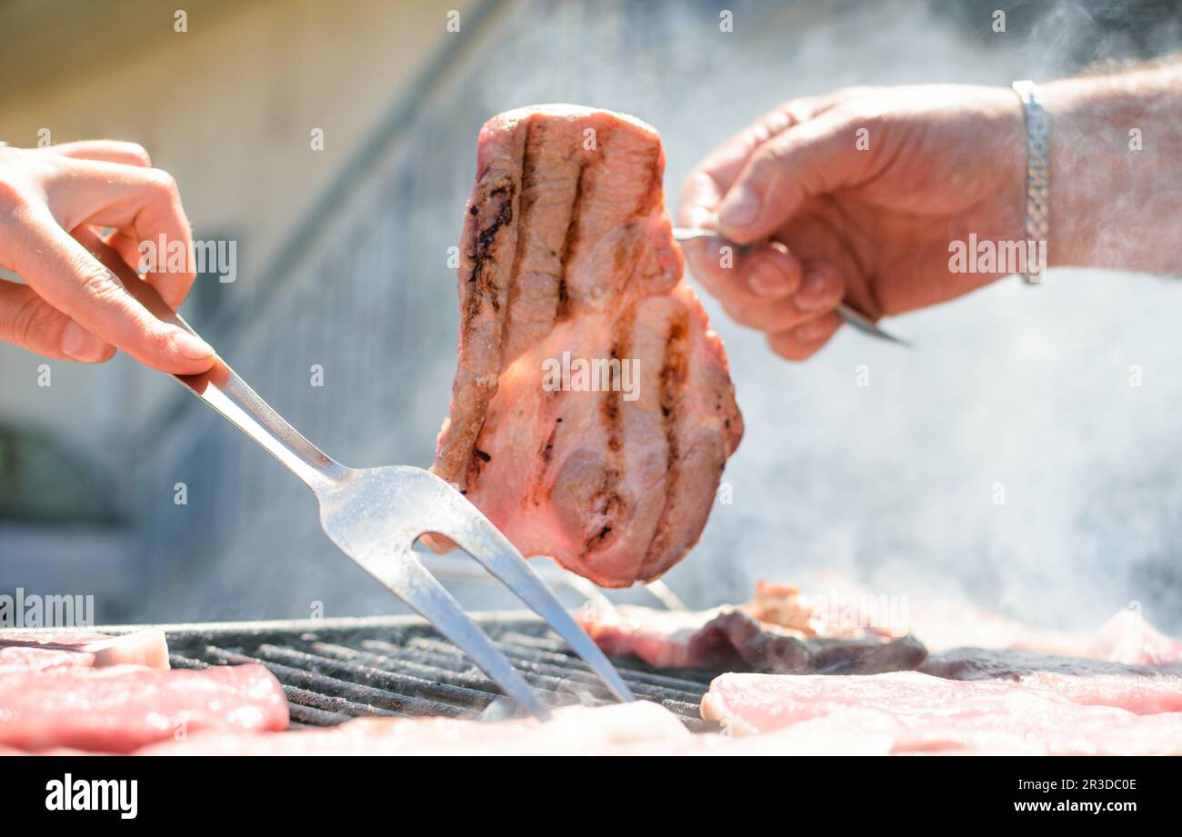 Hand holding steak cooking on smoking barbecue on terrace Stock Photo ...