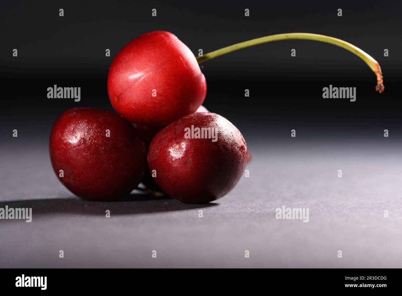 four ripe red cherries in an unusual pose on a dark background with ...