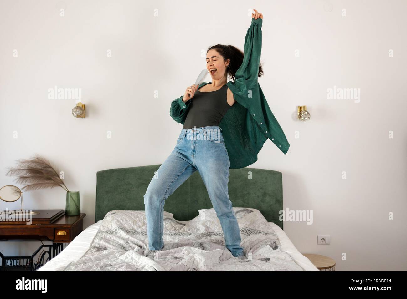 Young Caucasian happy woman is singing and dancing on bed. Funny enjoy ...