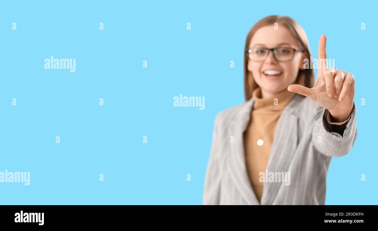 Laughing young businesswoman showing loser gesture on light blue ...