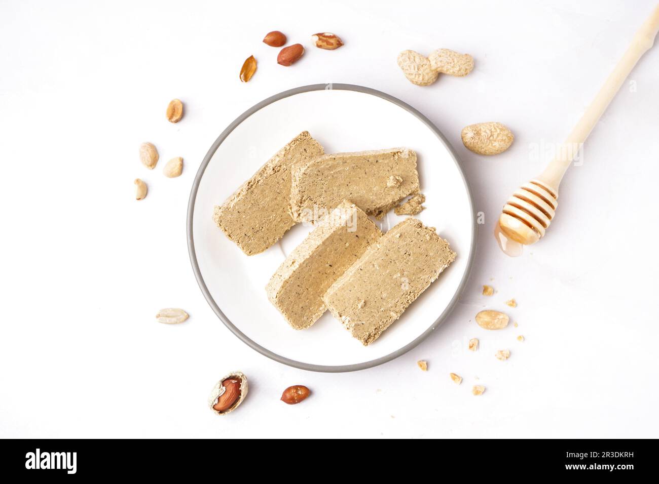 Plate with slices of tasty halva, peanuts and honey dipper on white background Stock Photo - Alamy