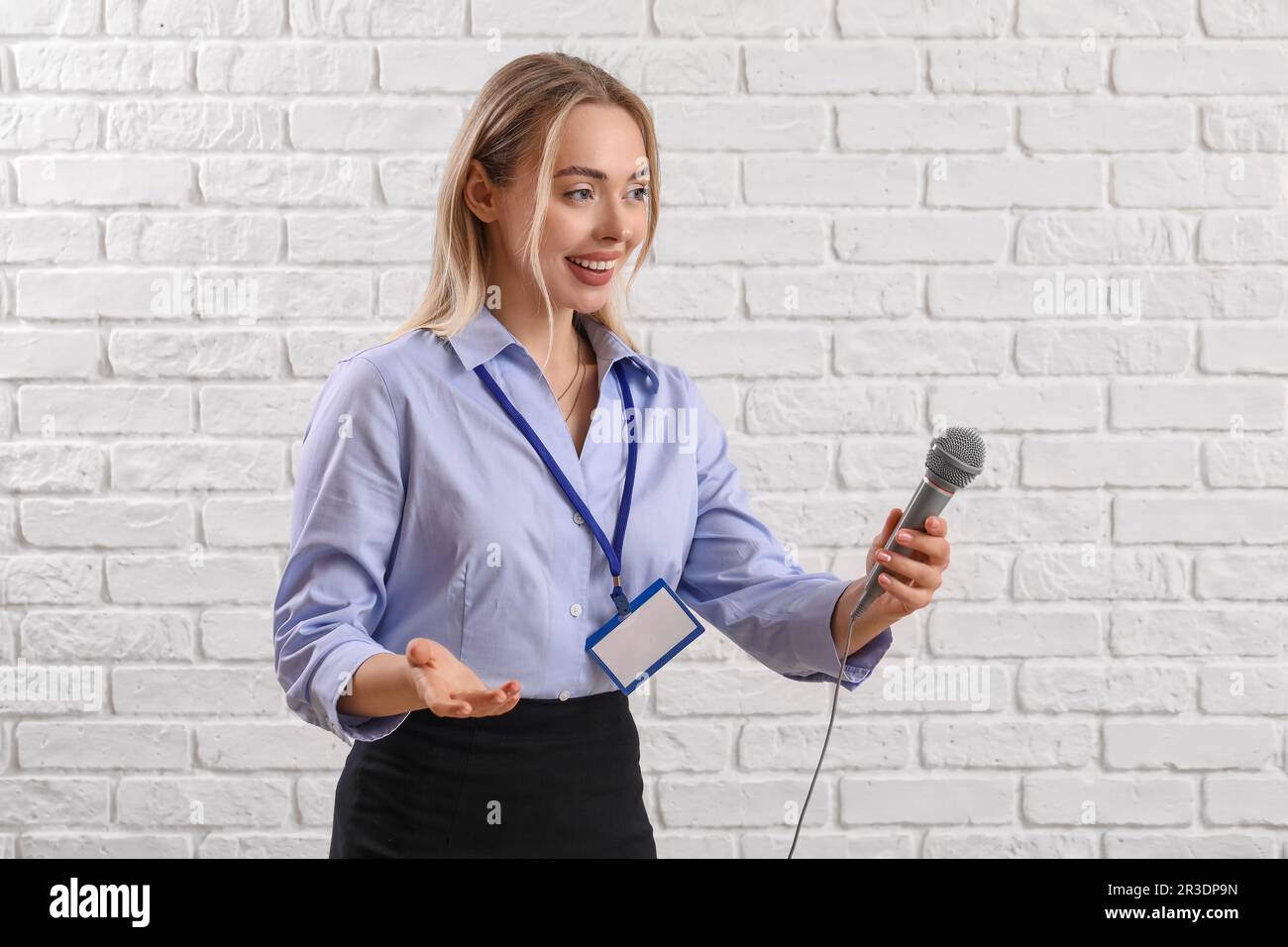 Female journalist with microphone on white brick background Stock Photo ...
