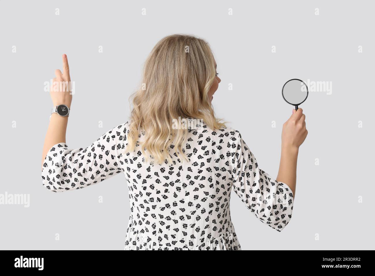 Young woman with magnifier pointing at something on light background ...