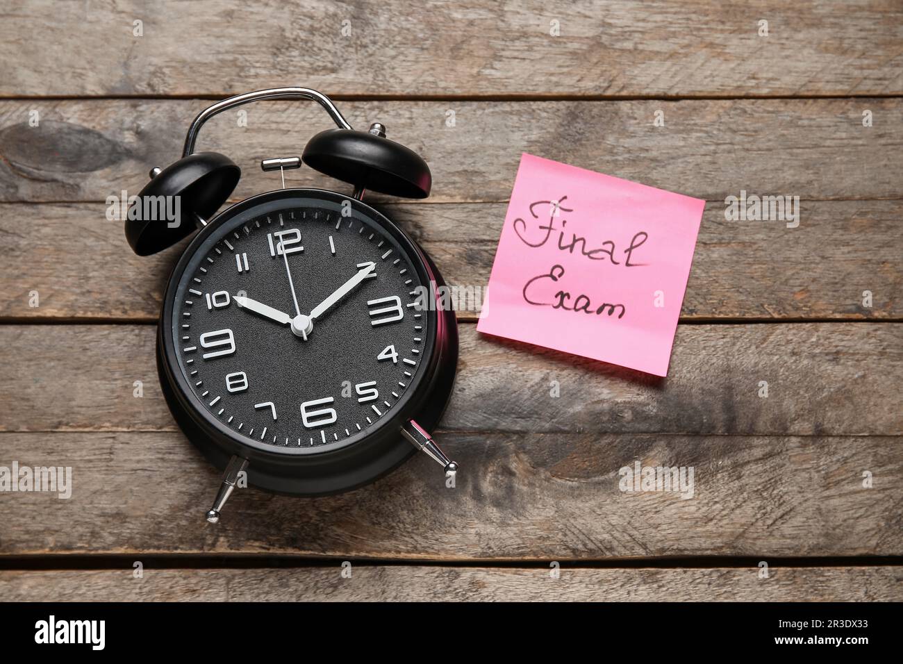 Sticky note with text FINAL EXAM and alarm clock on brown wooden ...