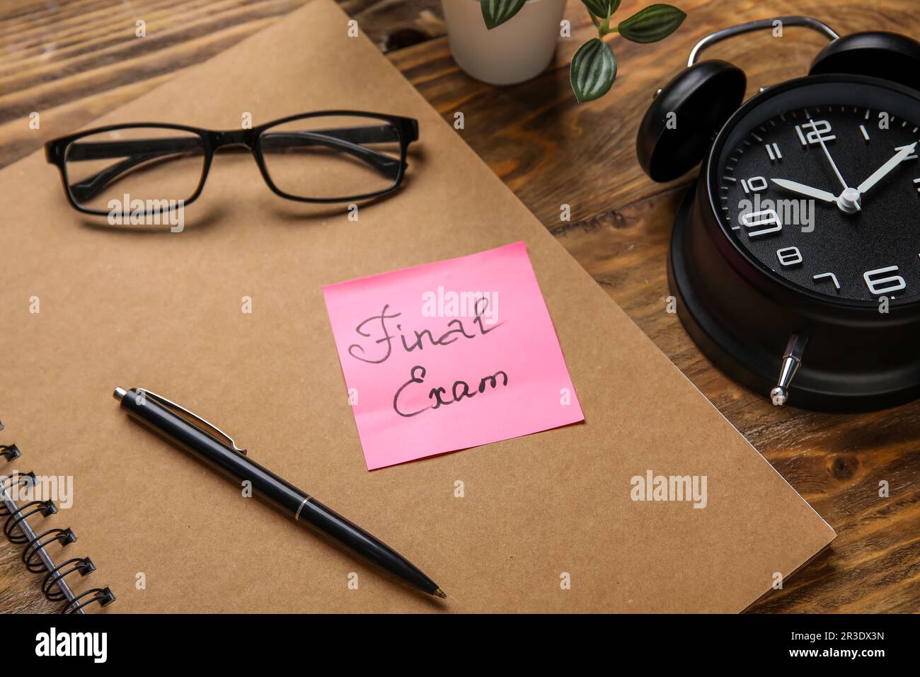 Sticky note with text FINAL EXAM, notebook, eyeglasses and alarm clock ...