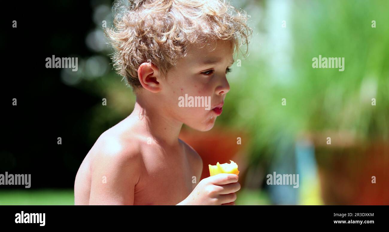 Cute toddler boy eating fruit snack outdoors in sunlight. Child chewing ...