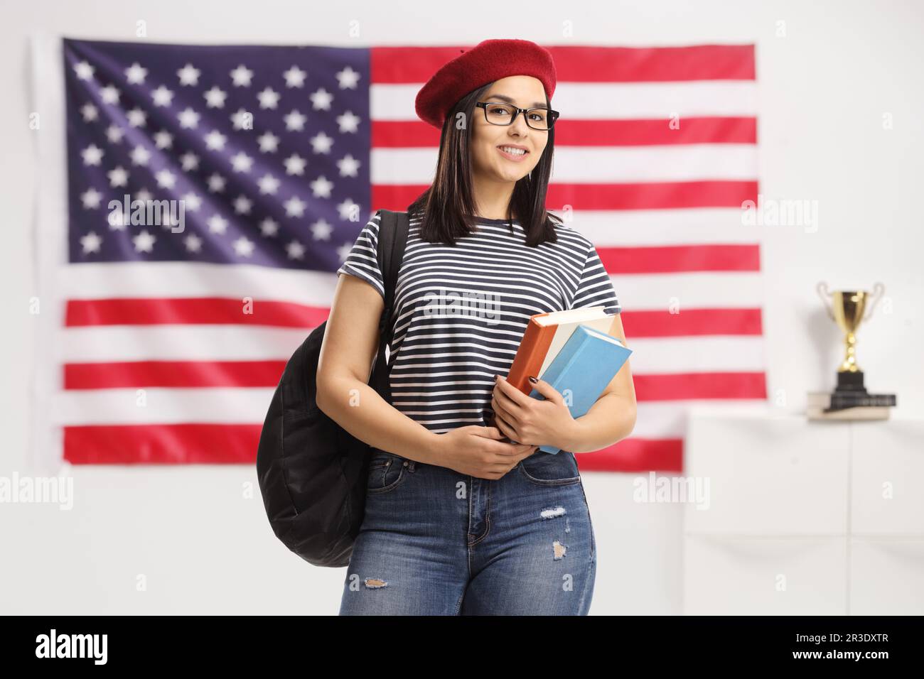 Female student posing with books in her hands in front of a USA flag ...