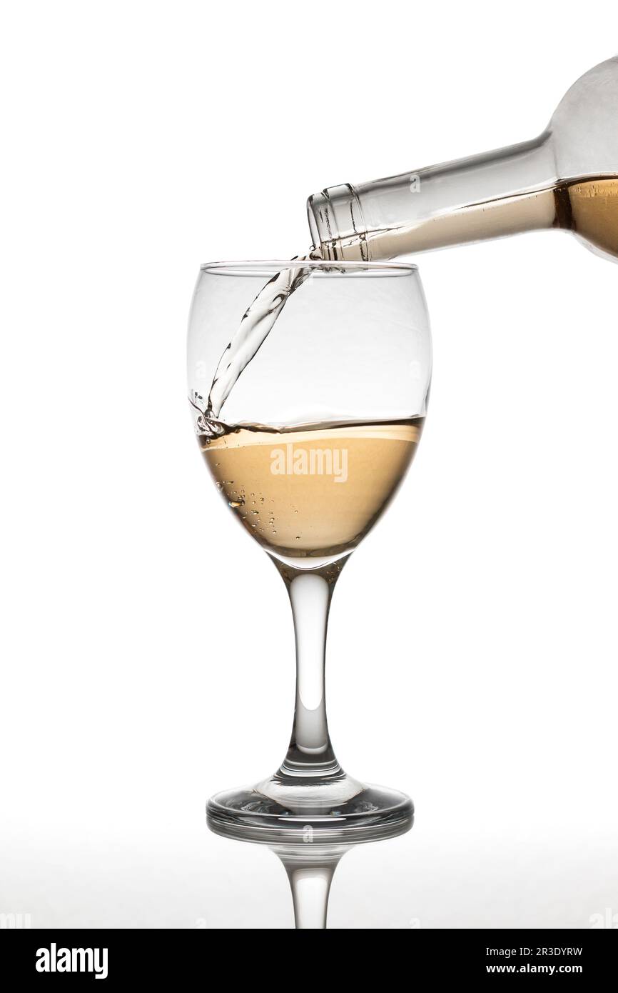 A bottle filling a white wine glass over a reflective surface over a ...