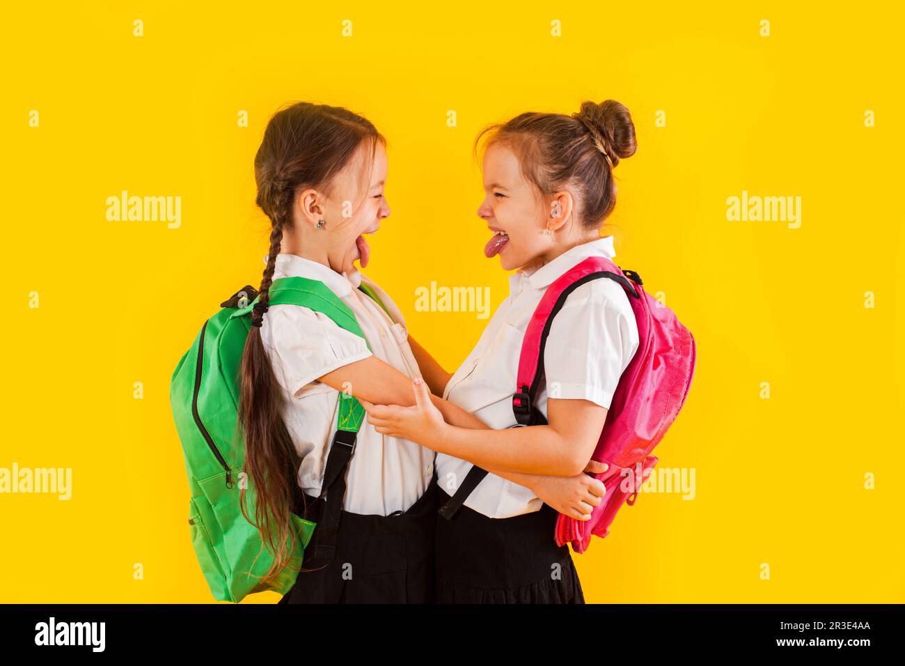 Two smiling schoolgirls in uniform are hugging at the yellow Stock ...