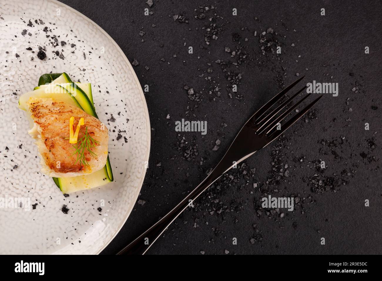 Grilled fish fillet served with zucchini on white plate over black ...