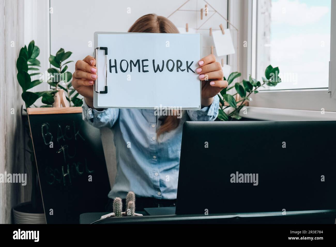 Young female teacher sitting at desk and using laptop showing HOMEWORK ...
